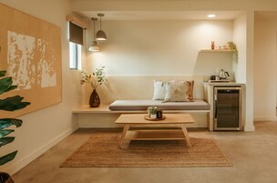 Uma sala de estar moderna com um sofá, uma mesa de centro, uma pequena cozinha com frigorífico e uma planta grande.