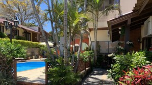 Uma área de piscina com deck de madeira, cercada por plantas tropicais e palmeiras.