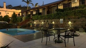Uma área de piscina com espreguiçadeiras e uma mesa, cercada por um muro de pedra e vegetação.