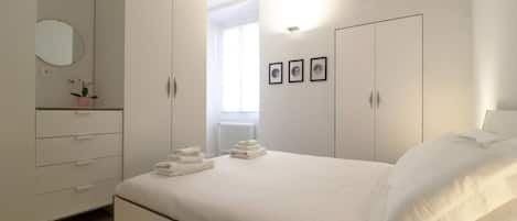 Quarto com cama, guarda-roupa, radiador e janela.