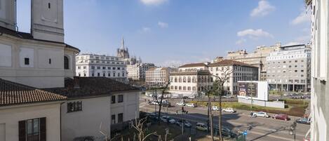 Paisagem urbana com edifícios históricos, uma torre do relógio imponente e uma rua movimentada com carros e pedestres.