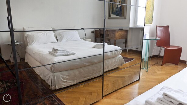 Um quarto com cama, escrivaninha, cadeira e mesa de vidro.