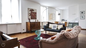 Uma sala de estar com um piano, uma mesa de centro de vidro, um sofá e um tapete vermelho.