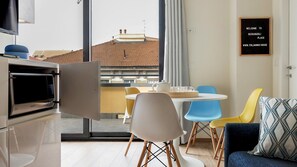 Cozinha moderna com micro-ondas, área de refeições com mesa e cadeiras, sofá e varanda com vista para edifícios.