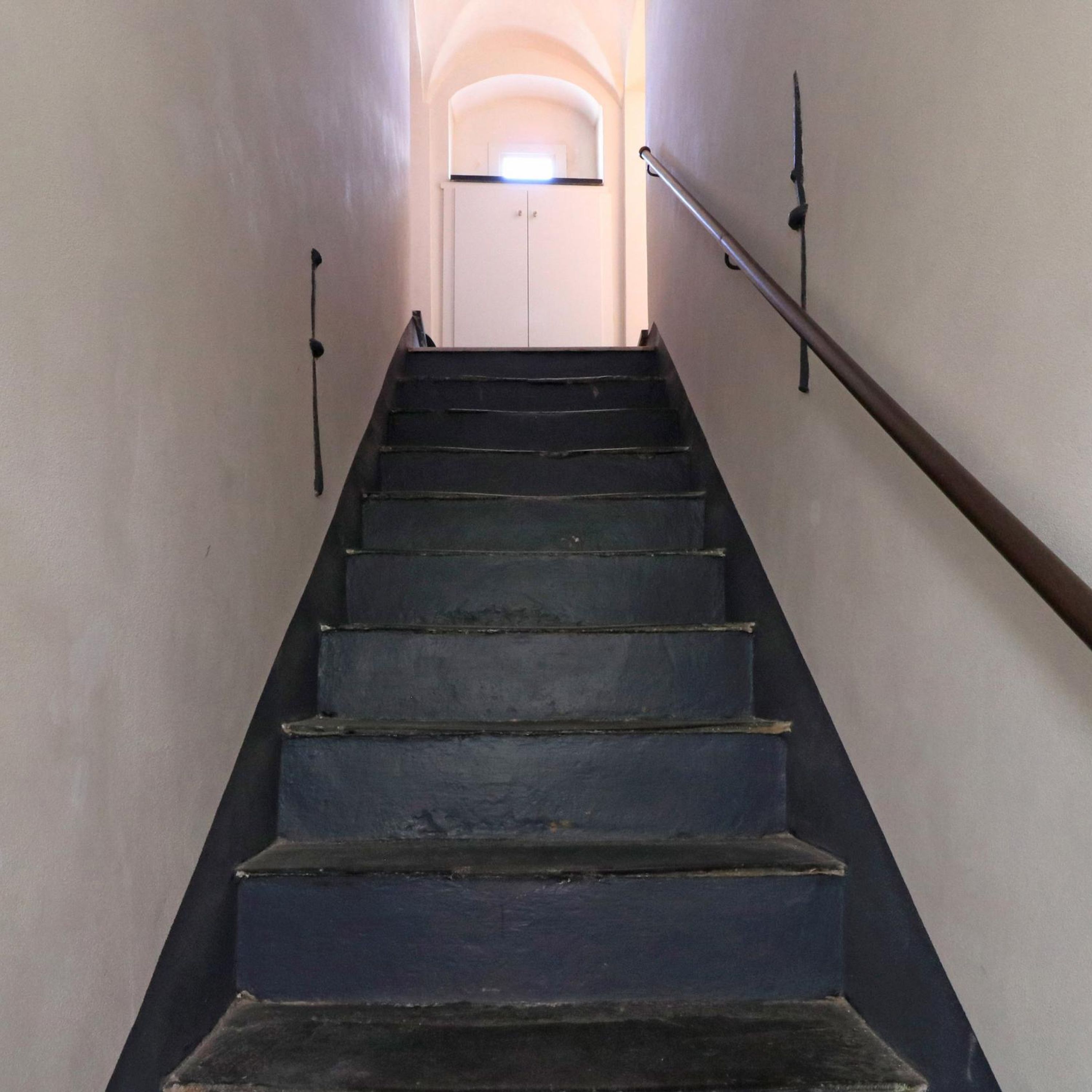 Uma escadaria com degraus pretos que levam a uma porta branca no topo.