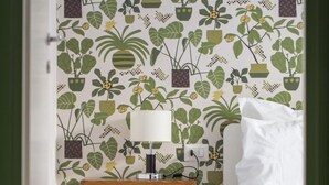 Quarto com papel de parede estampado, mesa de cabeceira com abajur e cama com roupa de cama branca.