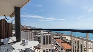 Varanda com mesa branca e duas canecas brancas, com vista para área costeira, edifícios e praia.