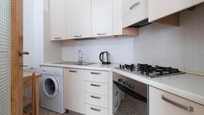 Cozinha compacta com máquina de lavar, fogão a gás e chaleira.