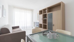 Uma sala de estar moderna com uma mesa de centro de vidro, um sofá, uma televisão e um armário de madeira.