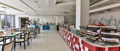 Um restaurante moderno com área de buffet, mesas compridas e cadeiras.