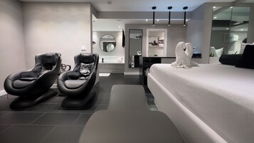 Quarto de hotel moderno com uma cama grande, duas cadeiras de massagem, uma banheira e um espelho.
