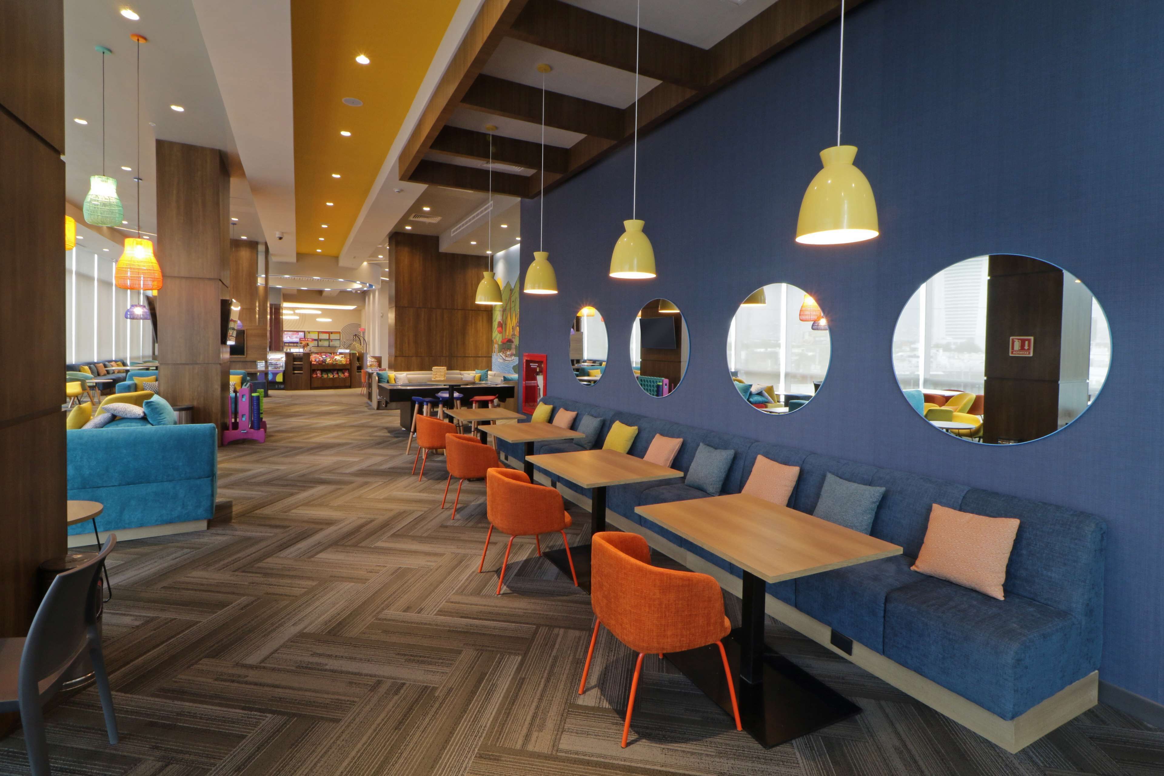 Um restaurante moderno com assentos azuis, cadeiras laranja e luminárias pendentes amarelas.