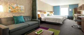 Quarto de hotel com sofá, duas camas, escrivaninha e uma cadeira.