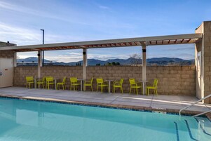 Área da piscina com espaço coberto para sentar, cadeiras e vista para montanhas.