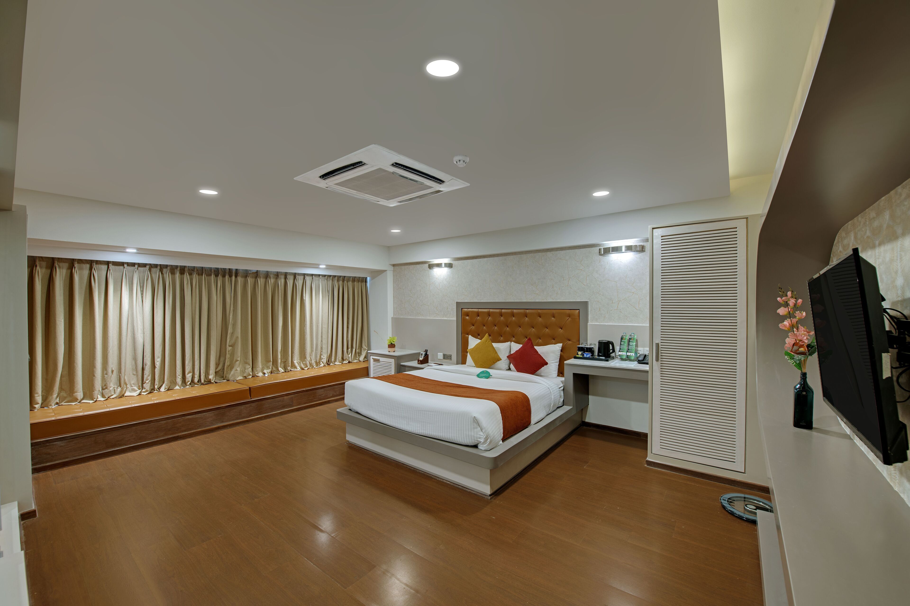 Quarto de hotel com uma cama, mesas de cabeceira, televisão e janela com cortinas.