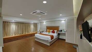 Quarto de hotel com uma cama, mesas de cabeceira, televisão e janela com cortinas.