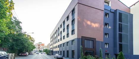 Um edifício moderno com fachada combinando tijolo e concreto, várias janelas e uma calçada vermelha.