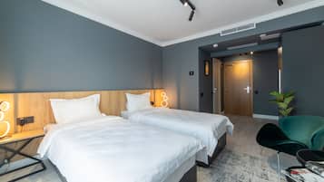 Quarto de hotel moderno com duas camas, uma mesa e uma cadeira verde.