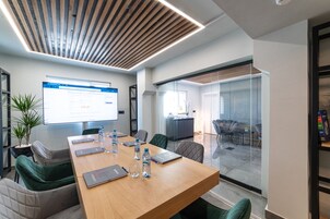 Uma sala de reunião moderna com uma mesa comprida, cadeiras, tela de projetor e um painel de vidro.
