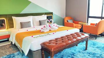 Quarto de hotel com uma cama, um banco, uma cadeira, uma mesa pequena e uma janela.