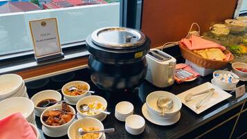 Disposição de buffet com diversos pratos, uma máquina de café e uma placa indicando 'PLAIN Porridge'.