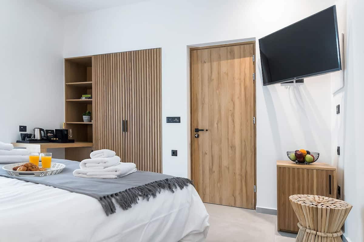 Quarto de hotel moderno com uma cama, um guarda-roupa de madeira, uma TV de tela plana, um pequeno armário de madeira e uma mesa de cabeceira com uma cesta de frutas.