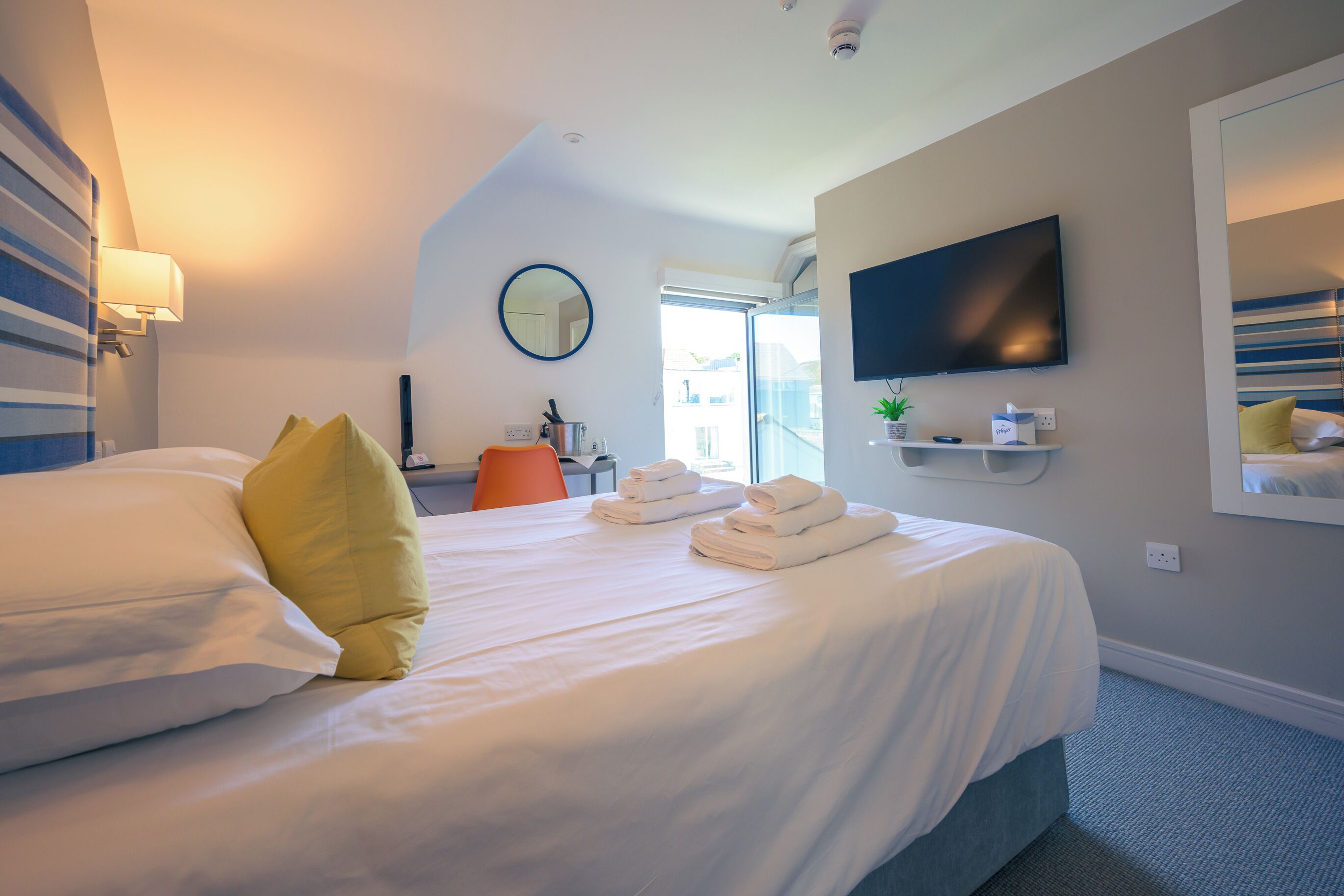 Quarto de hotel com cama, televisão, espelho e janela.