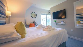 Quarto de hotel com cama, televisão, espelho e janela.