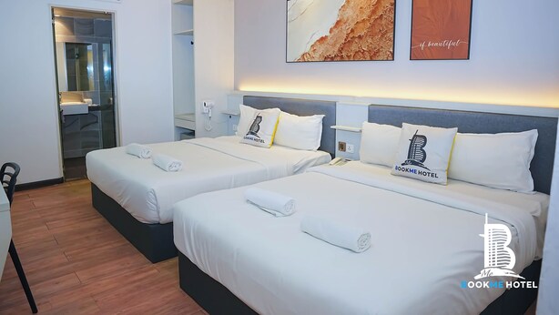 Quarto de hotel com duas camas, uma mesa e uma cadeira. Há duas fotos emolduradas na parede, uma mesa de cabeceira com abajur e um telefone fixado na parede.