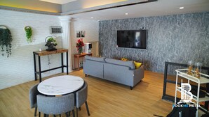 Quarto de hotel moderno com um sofá cinzento, uma mesa redonda de mármore e uma televisão fixada na parede.