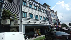 Hotel com fachada moderna, várias janelas e estacionamento com carros e uma van.