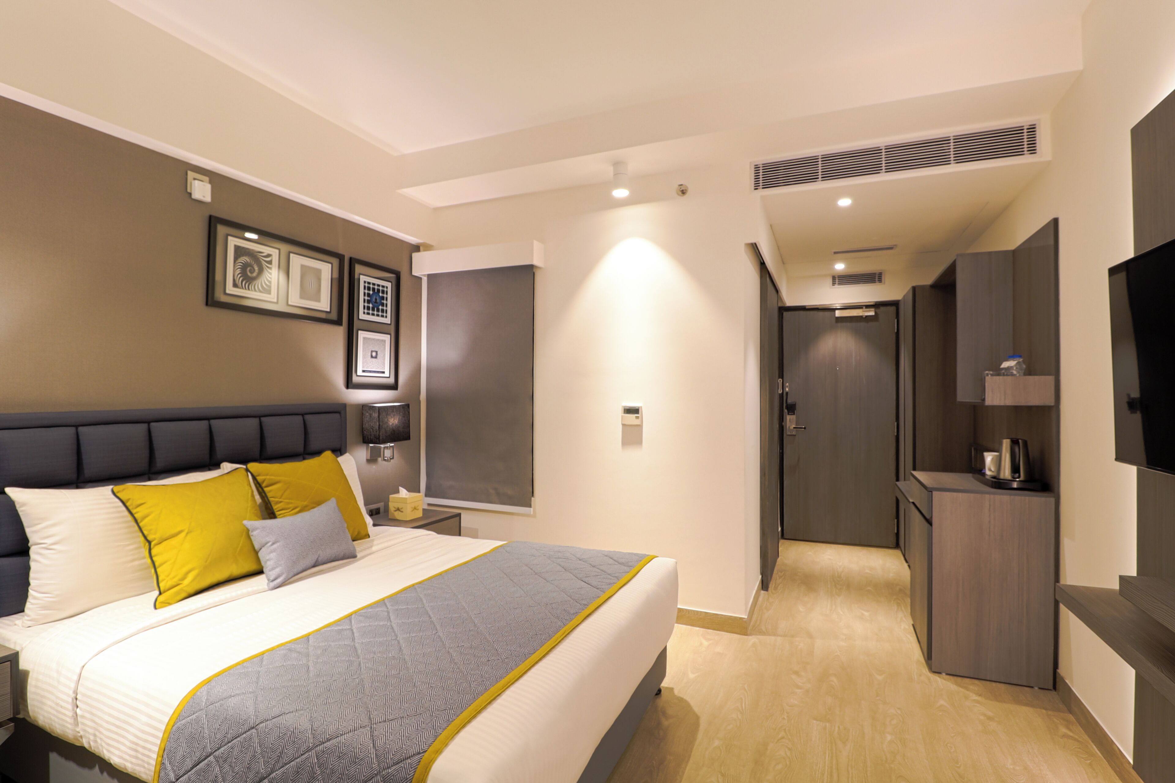Quarto de hotel moderno com uma cama grande, uma mesinha de cabeceira, televisão de tela plana e uma pequena cozinha.