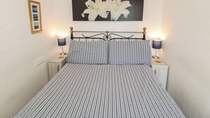 Uma cama bem arrumada com colcha estampada, duas luminárias de cabeceira, um quadro na parede e uma grande pintura floral acima da cama.