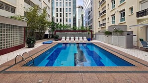 Piscina com deck revestido, rodeada por edifícios altos.