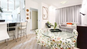Uma sala de estar moderna com uma mesa de centro de vidro, um sofá e um espaço de jantar com banquetas.