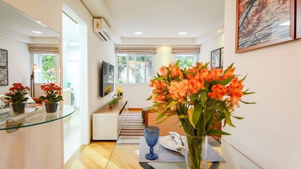 Um interior moderno com uma mesa de vidro, um vaso de flores e uma TV de tela plana fixada na parede.