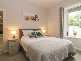 Quarto com cama, luminárias de cabeceira, mesa de cabeceira, janela com cortinas e uma obra de arte na parede.