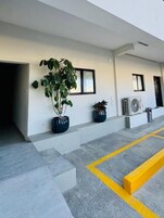 Fachada moderna de um edifício com linhas brancas e limpas, uma grande planta em vaso e uma linha de segurança amarela no pavimento.