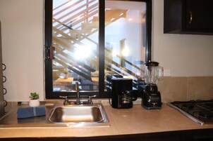 Uma cozinha com uma pia de aço inoxidável, uma cafeteira e um liquidificador na bancada.