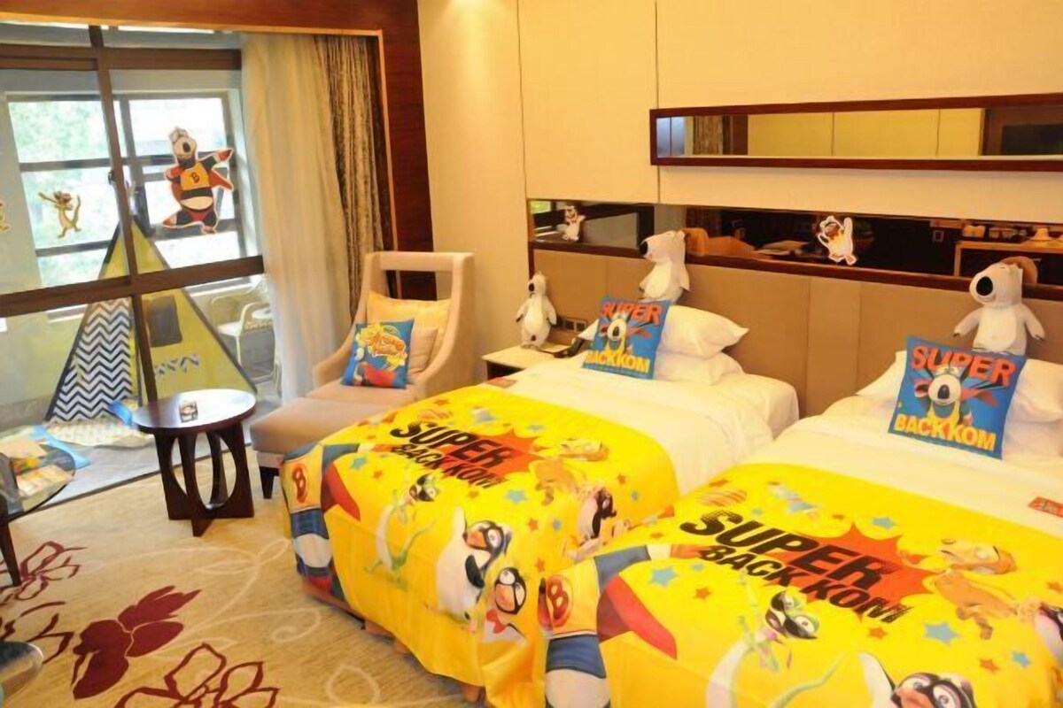 Quarto de hotel com duas camas, uma mesa pequena, uma cadeira e uma janela com cortinas.