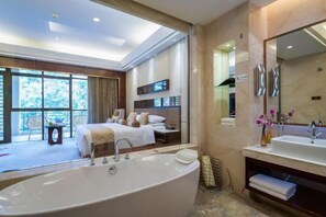 Quarto de hotel moderno com uma banheira grande, uma cama com roupa de cama branca, uma televisão na parede e uma varanda com área de estar ao ar livre.
