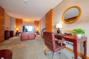 Quarto de hotel com escrivaninha, cadeira, televisão e um espelho grande na parede.
