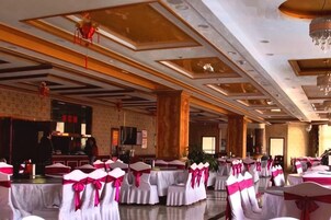 Salão de banquetes com mesas redondas, cadeiras com fitas cor-de-rosa e uma área de palco.