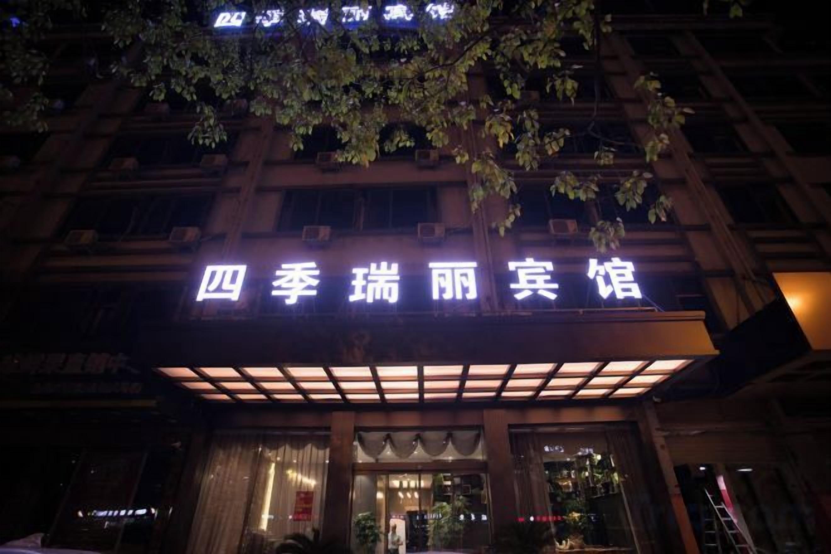 Entrada de hotel com placa em caracteres chineses, área de acesso coberta e uma árvore acima.
