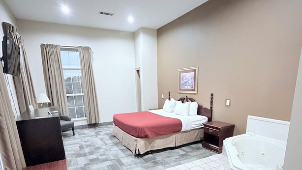 Quarto de hotel com cama, secretária, cadeira, televisão, janela e banheira.