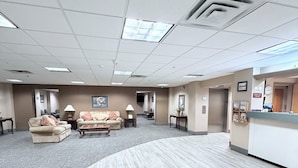 Um hall amplo com um balcão de recepção curvo, área de estar com sofás e teto revestido com azulejos e iluminação embutida.