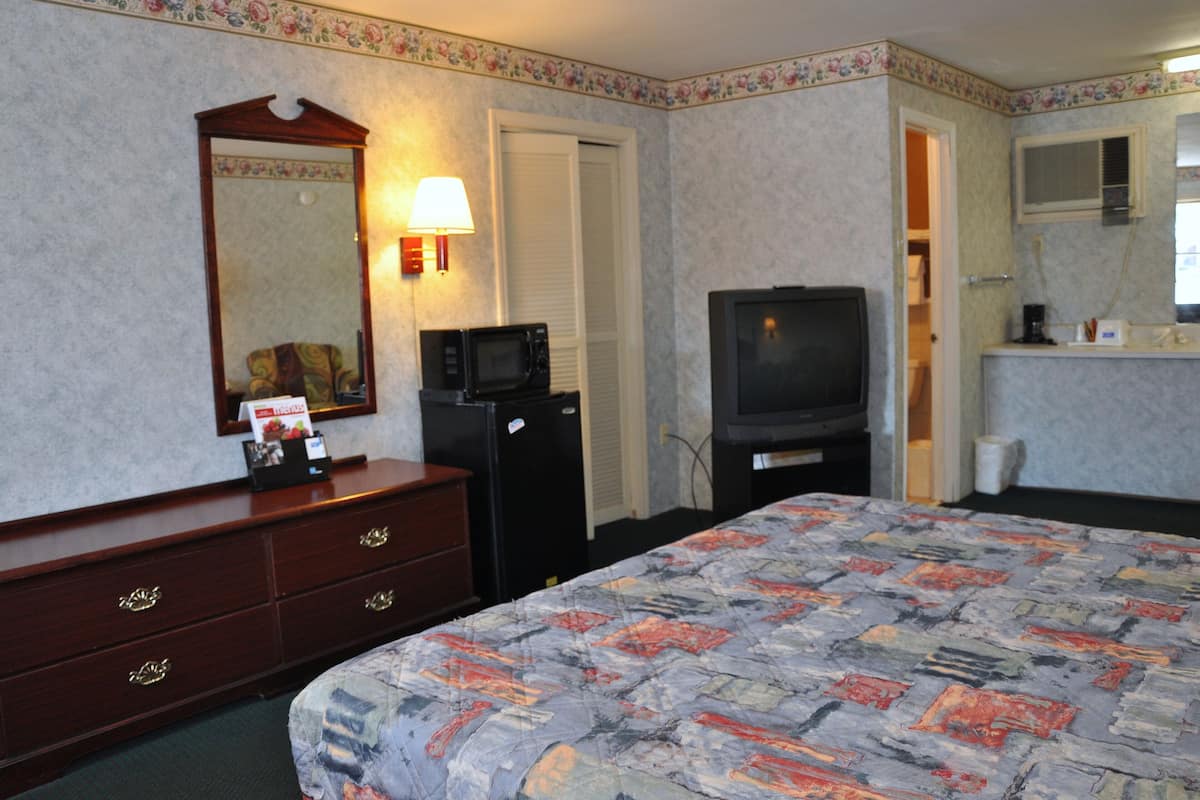 Quarto de hotel com cama, penteadeira, televisão, micro-ondas e banheiro visível através de uma porta aberta.