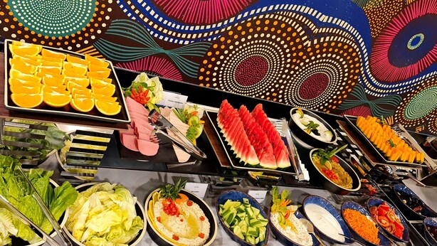 Buffet com diversos alimentos, incluindo fatias de laranja, melancia e diferentes saladas.