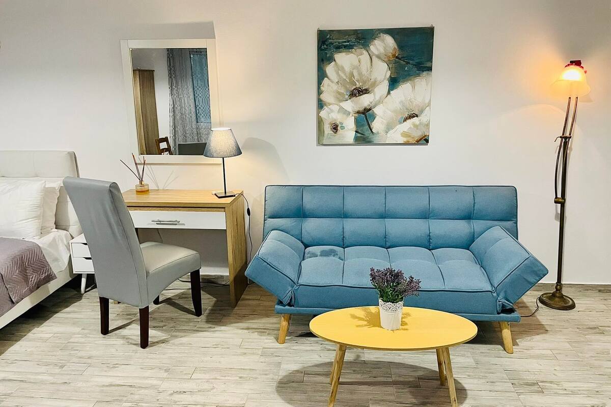 Quarto moderno com uma cama, uma escrivaninha, um sofá azul, uma pequena mesa redonda com um vaso e um abajur.