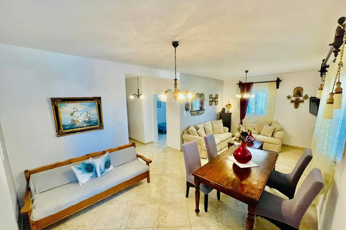 Uma sala de estar espaçosa, com uma mesa de jantar de madeira, um sofá e um lustre.